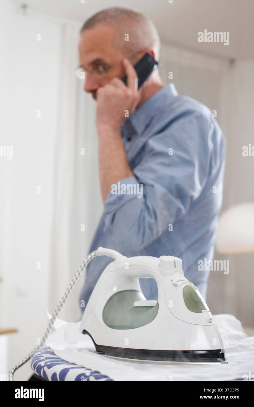 A man talking on the phone with his back to an iron which is burning ...