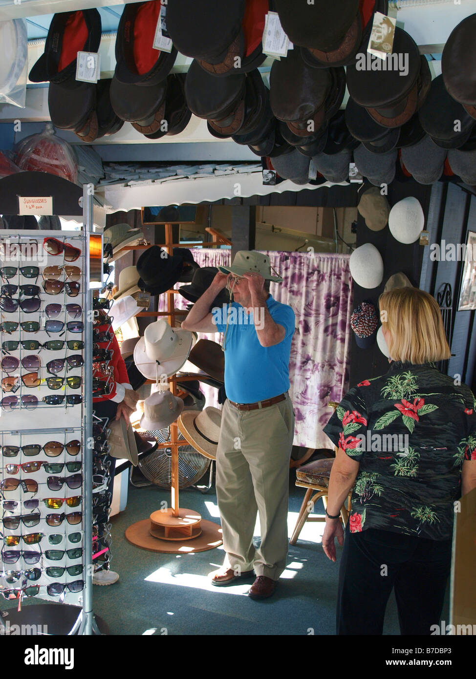 Senior man tries on hat in hat shop, while shopkeeper looks on Stock ...