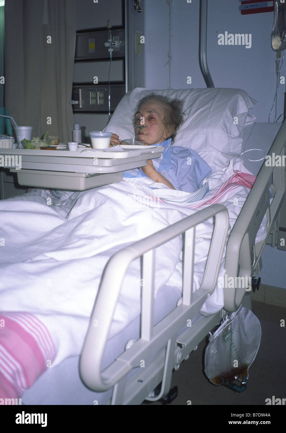 an old or elderly sick or ill woman in a hospital bed eating a meal ...