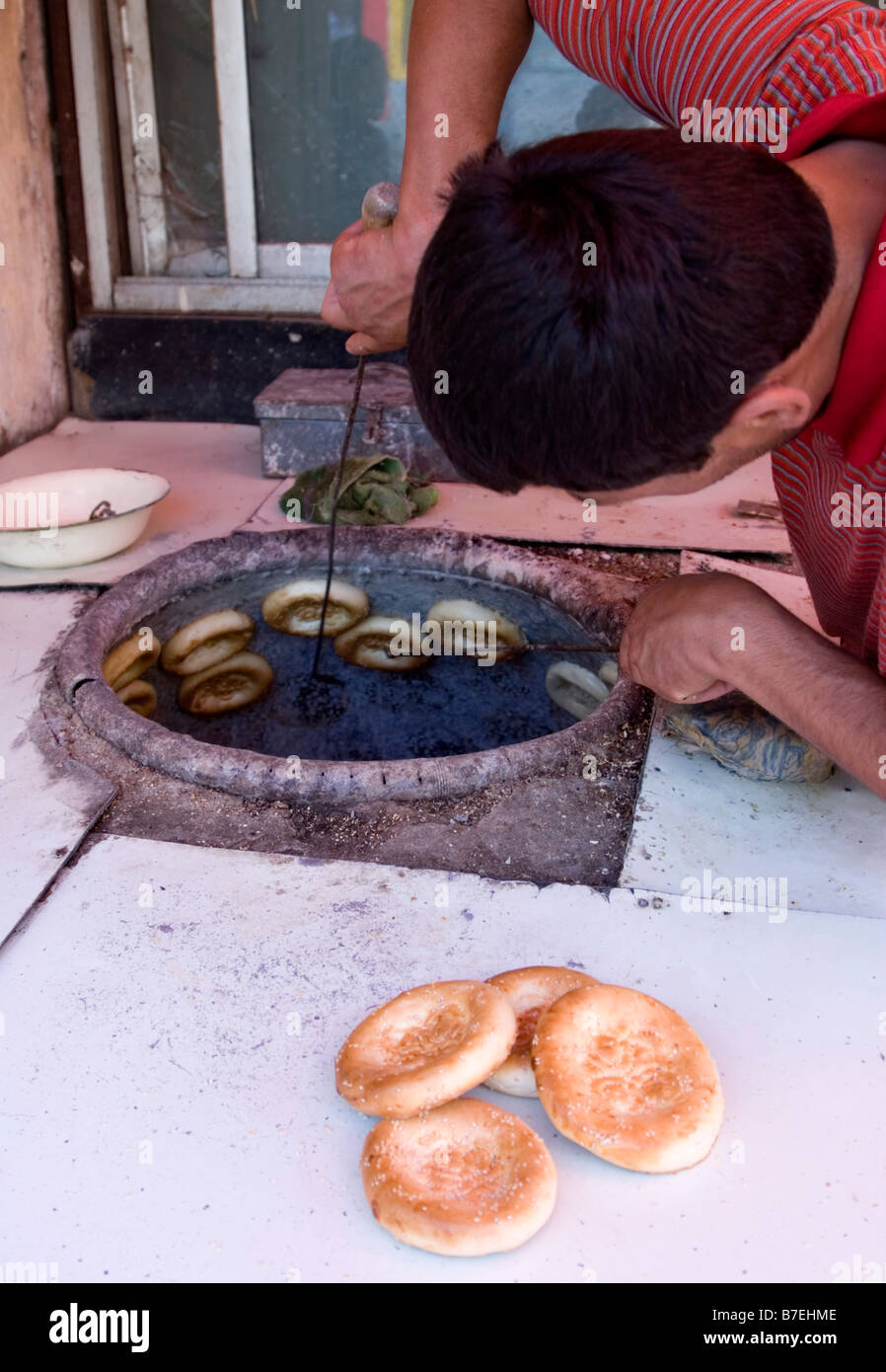 A baker baking bread in an oven or tandoor in Urumqi capital of ...