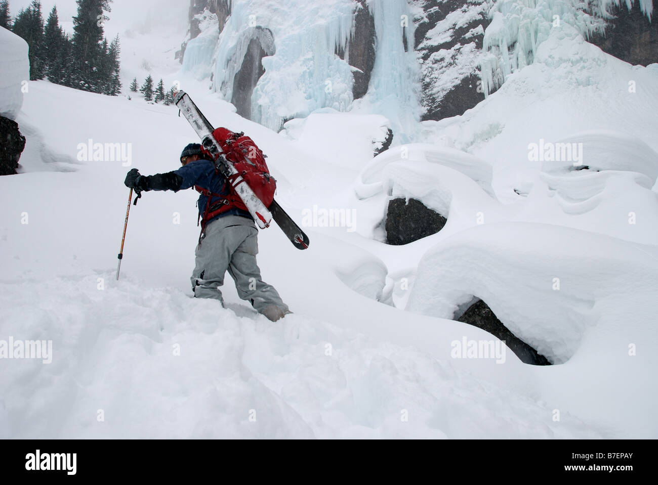 a backcountry skier climbs up past a frozen waterfall to ski deep ...