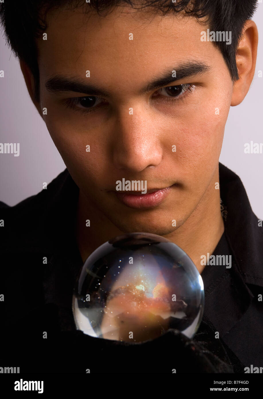 A young Asian American man staring into a crystal ball to see the ...