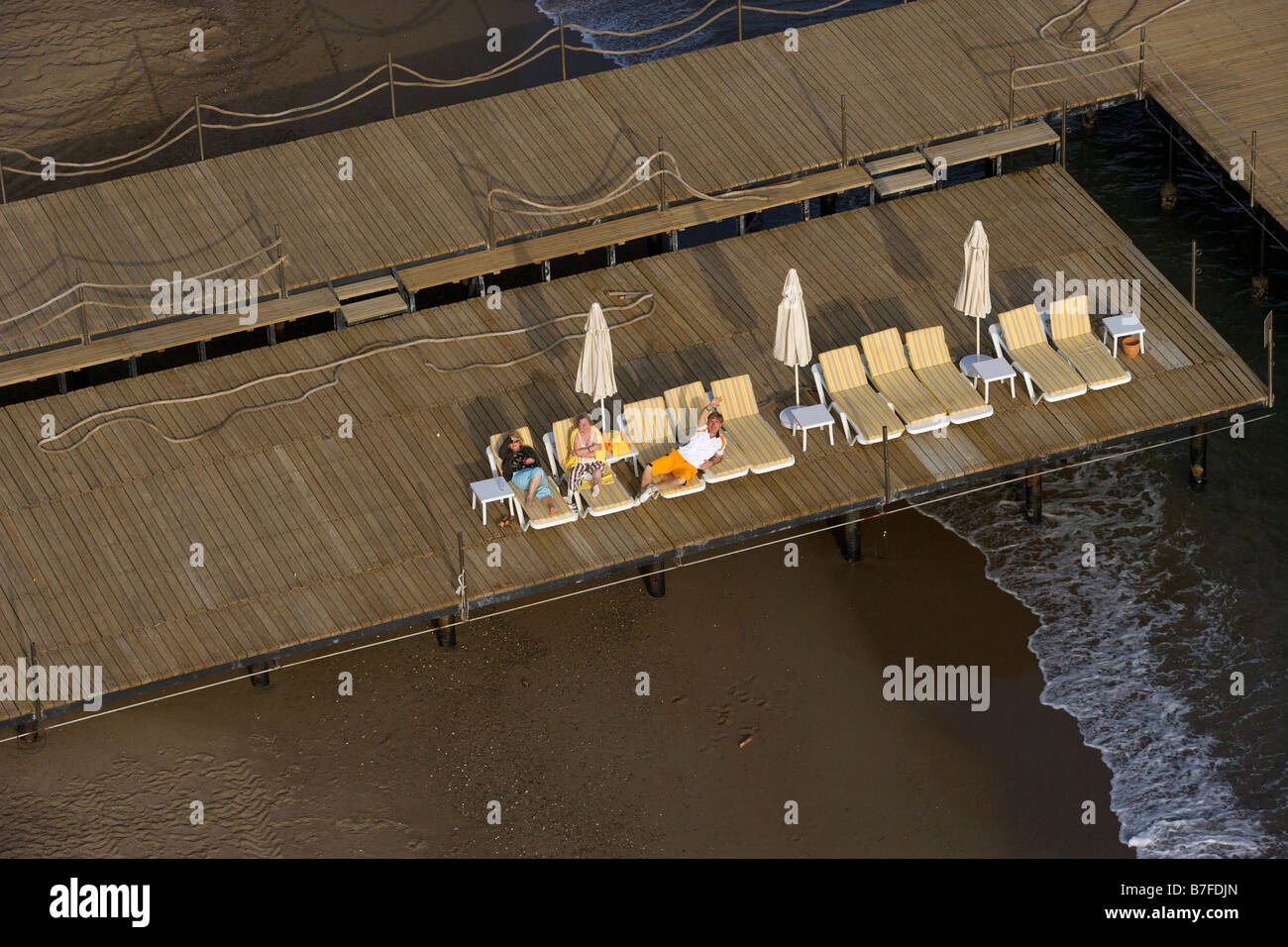 Aerial view of three people lying on reclining chairs on wooden pier ...
