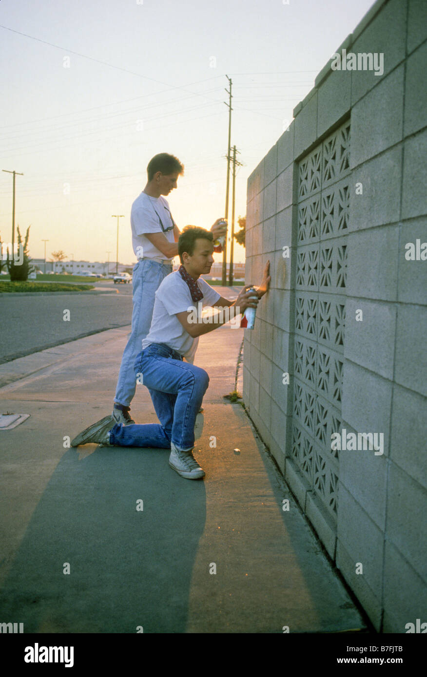 Two teen boys spray graffiti onto block wall vandal paint mark area ...