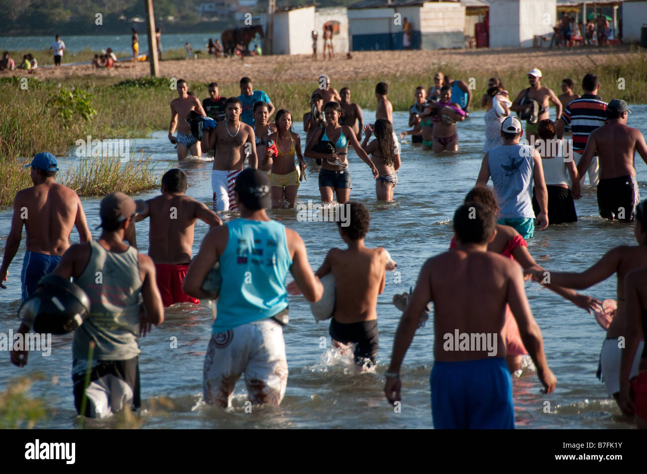 People walk through water to reach a river beach with a small number of ...