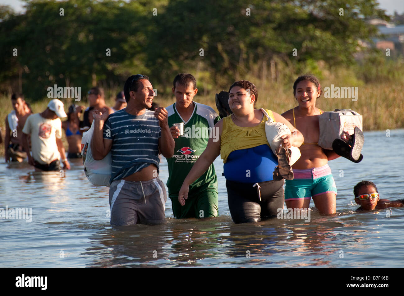People walk through water to reach a river beach with a small number of ...