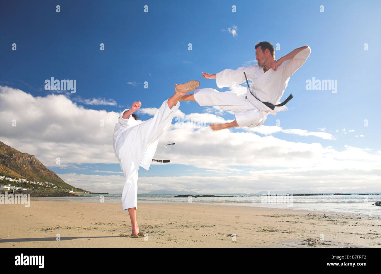 Young adult men practicing Karate on the beach One is in a high kick ...