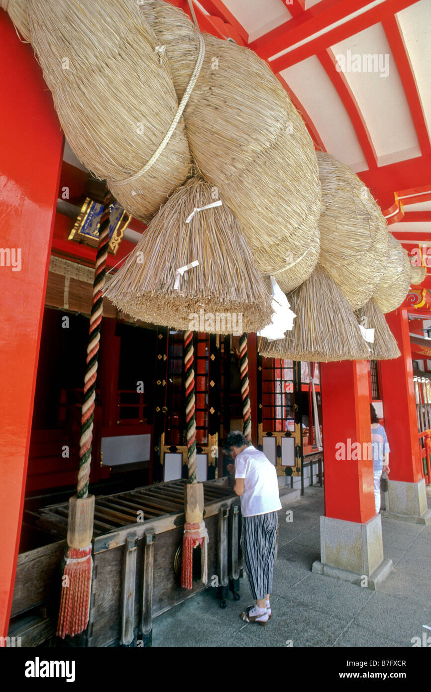 A visitor prays beneath large braided straw rope Taikodani Inari jinja ...