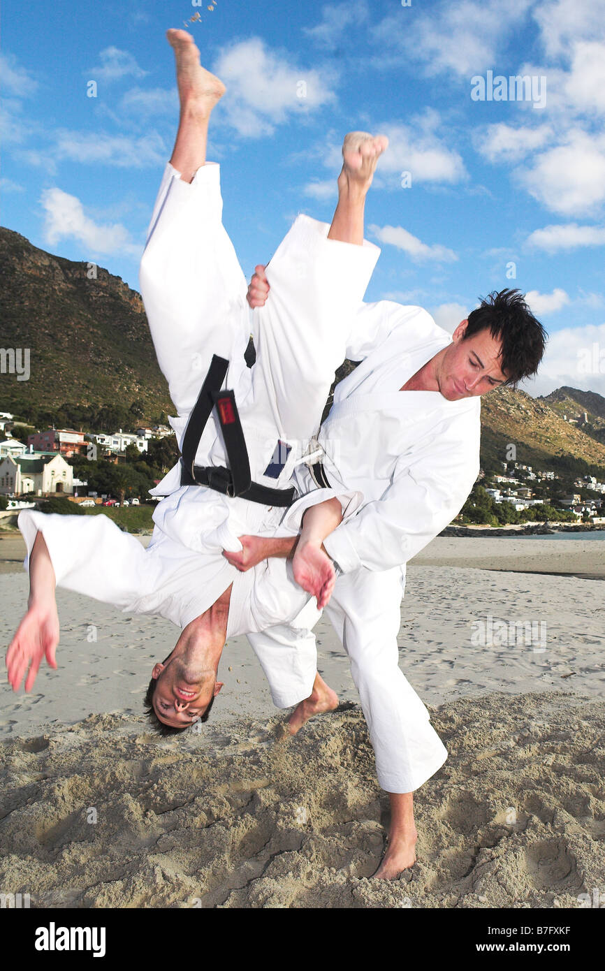 Young adult men with black belt practicing fighting on the beach on a ...