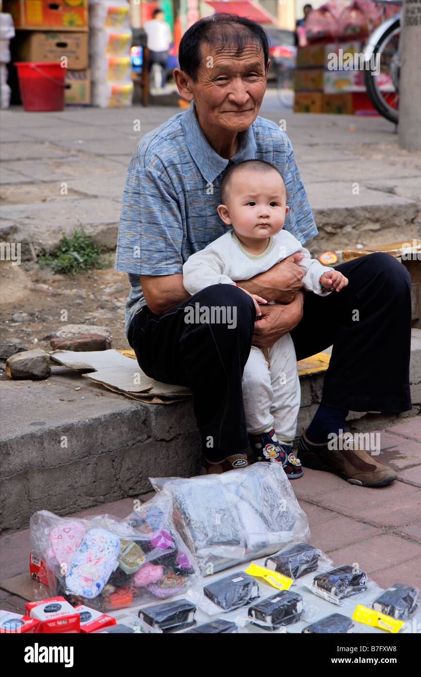 An elderly Chinese man with a young Chinese boy sitting in a street of ...