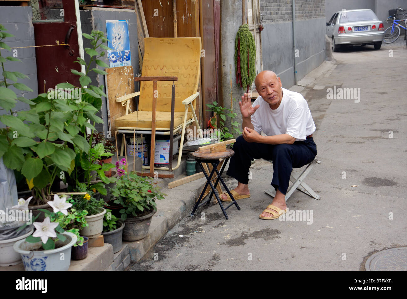 A friendly Chinese man sitting in front of his house in a narrow alley ...