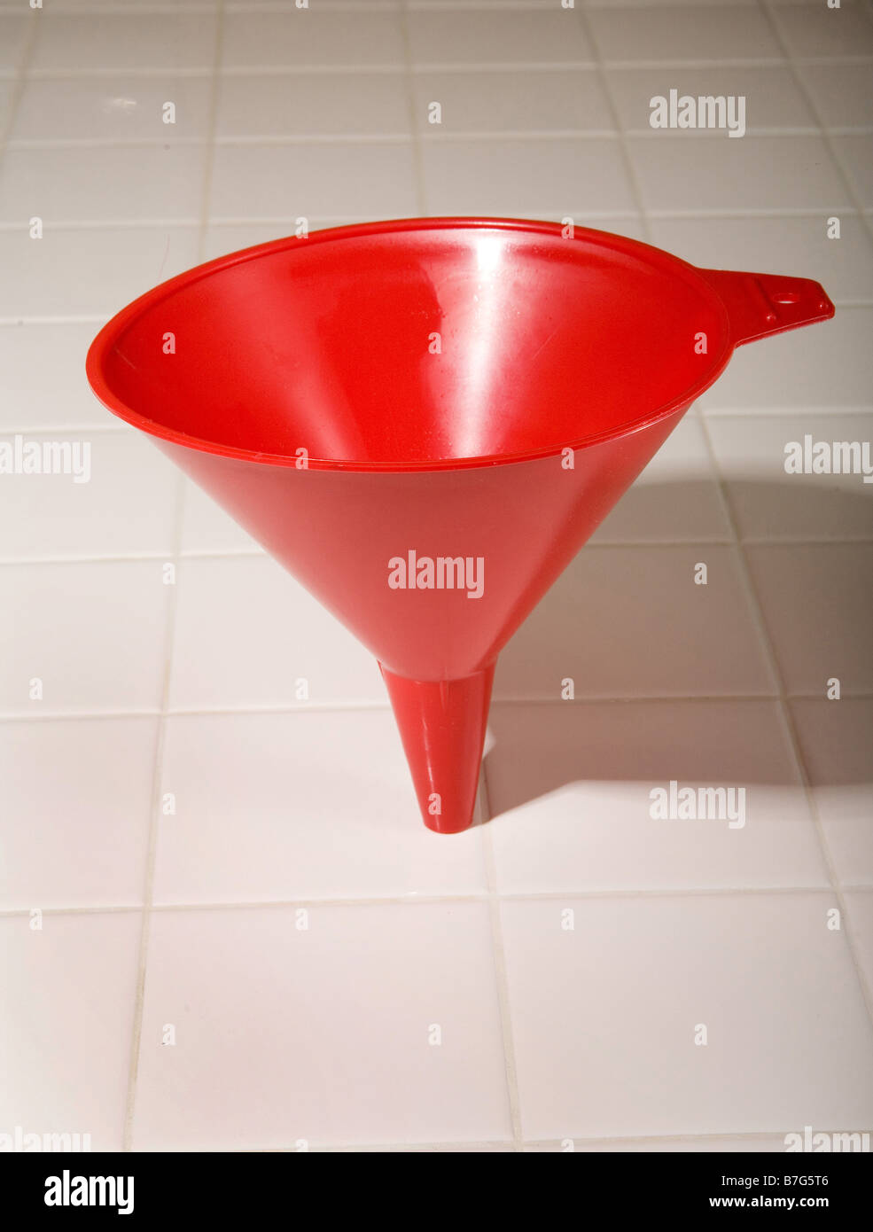 Red plastic funnel sits on tip on white tile surface oil Stock Photo ...