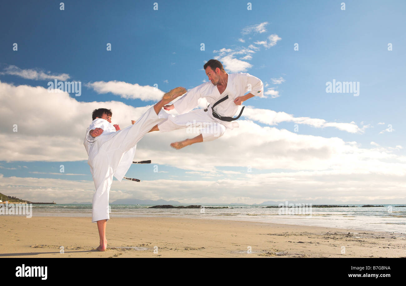 Young adult men practicing Karate on the beach One is in a high kick ...