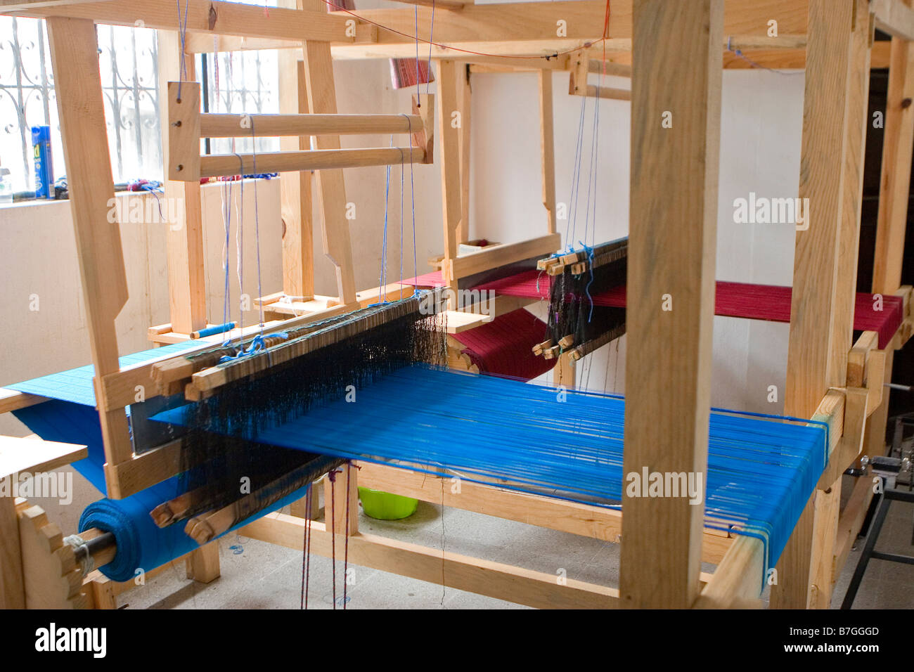Large free standing loom with bright blue yarn in a woman's cooperative ...