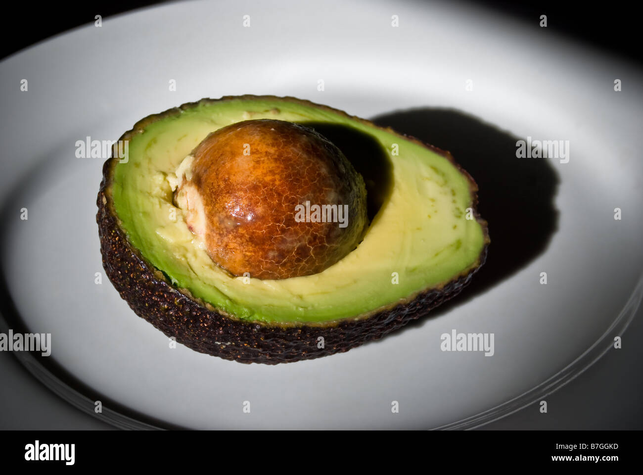 Half avocado on the white plate Stock Photo - Alamy