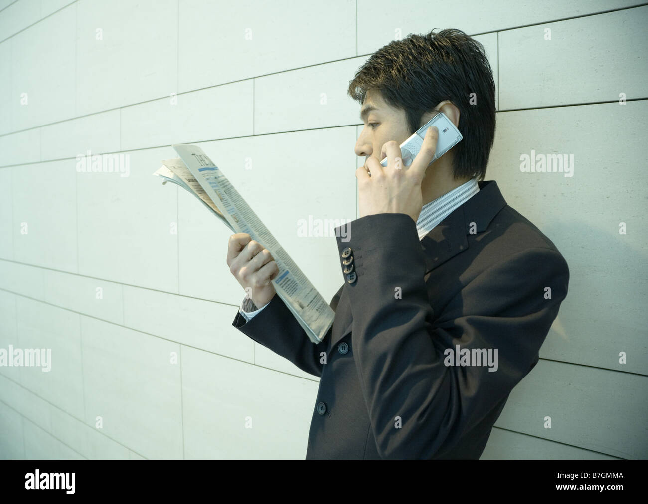 Man on cell-phone reading newspaper Stock Photo - Alamy