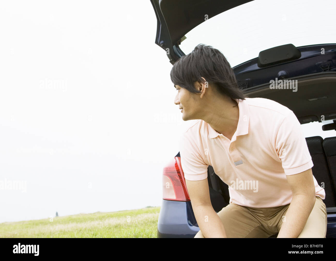 A young man leaning against a car trunk Stock Photo - Alamy
