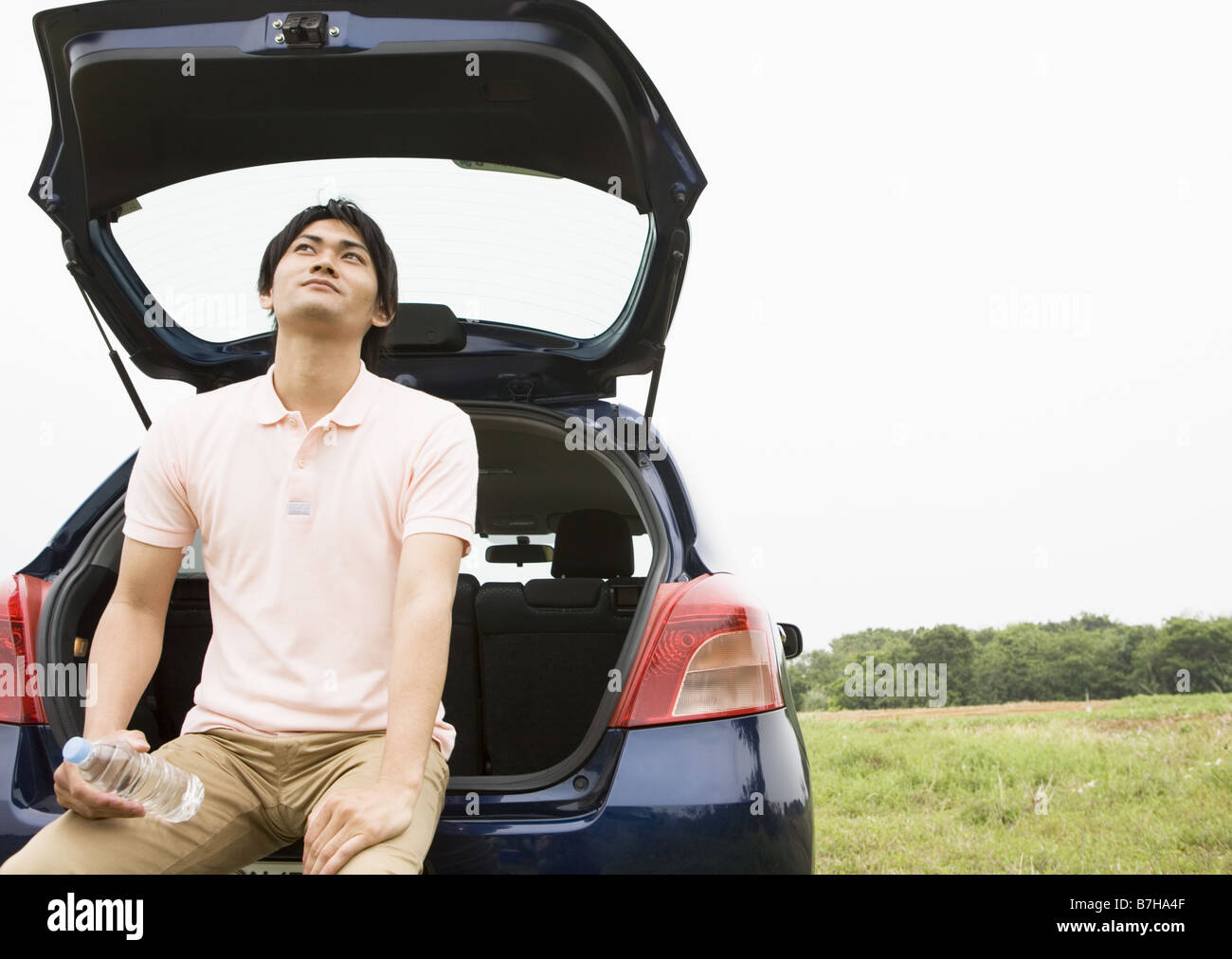 A young man leaning against a car trunk Stock Photo - Alamy