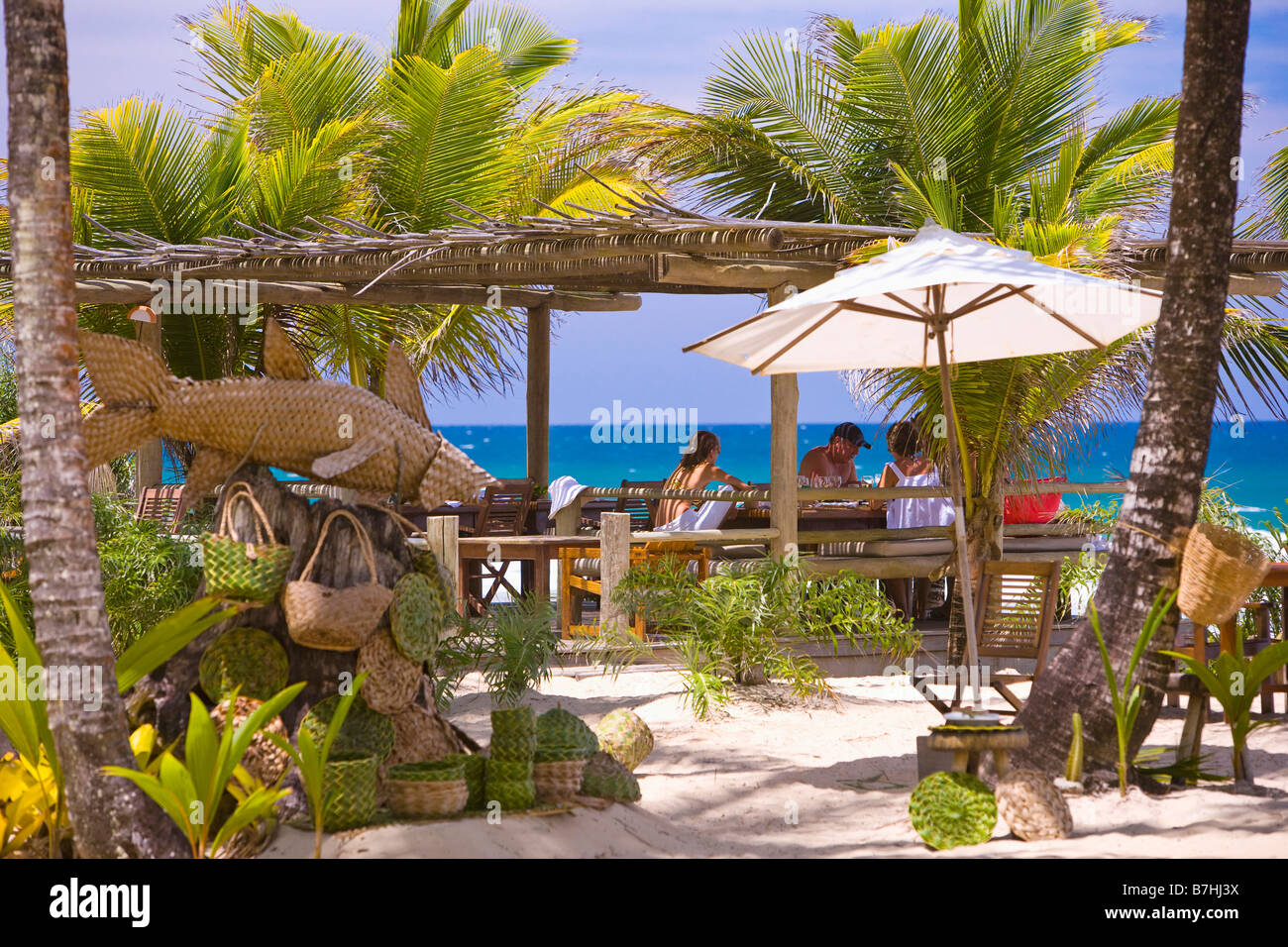People in rustic restaurant bar below palm trees overlooking beach in ...