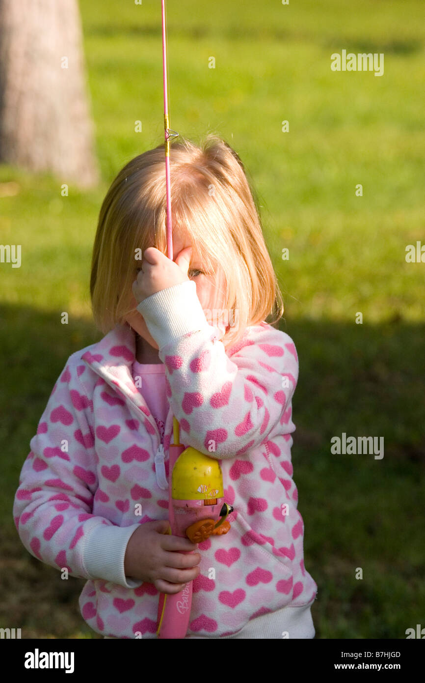 A shy young girl hiding behind her fishing pole at a fishing derby ...