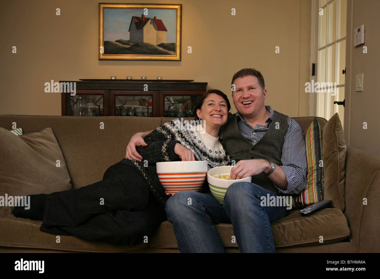 A couple relaxing and snacking while watching TV on their living room ...