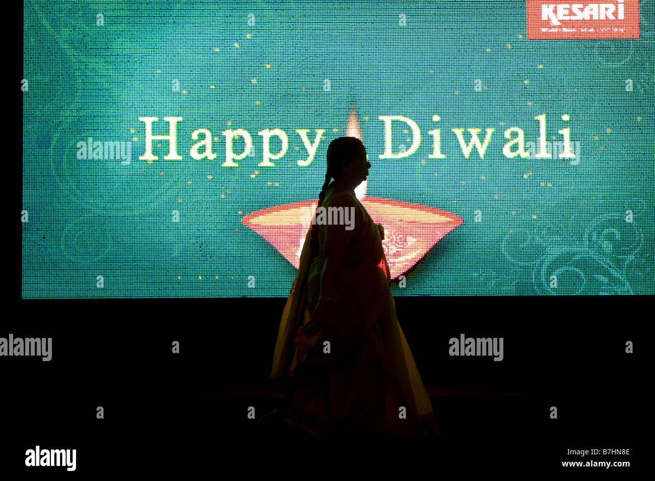 A silhouette of a woman walking in front of an electronic billboard ...