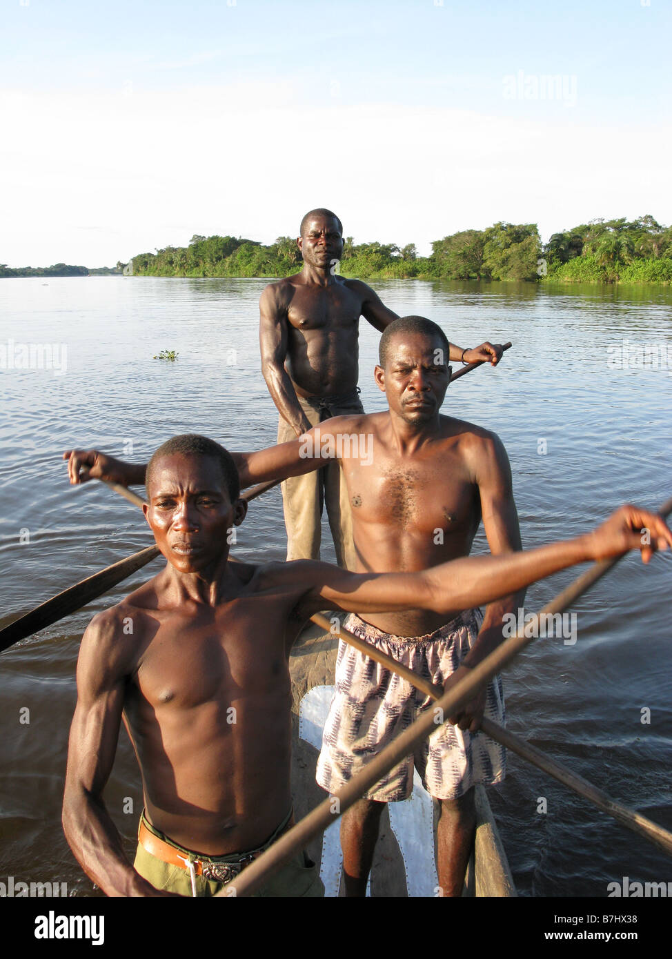 Three Lingala fishermen standing up to paddle large dugout canoe on ...