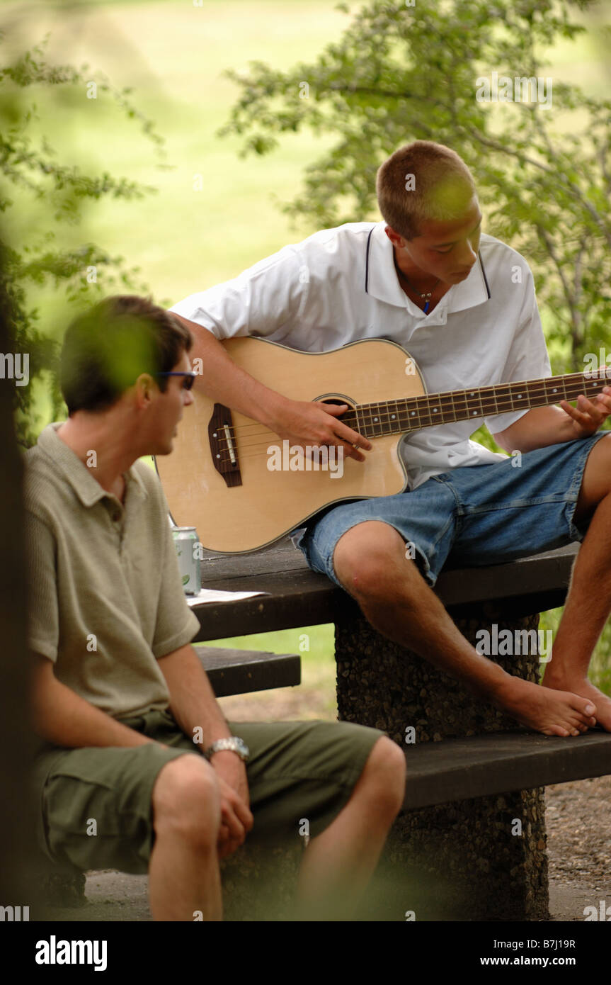 Young guys playing guitar sitting at picnic table, Regina, Saskatchewan ...