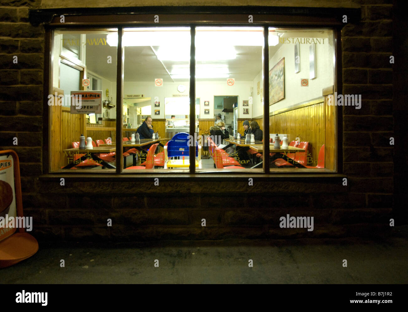 A brightly lit fish and chip shop in Matlock at night with people ...