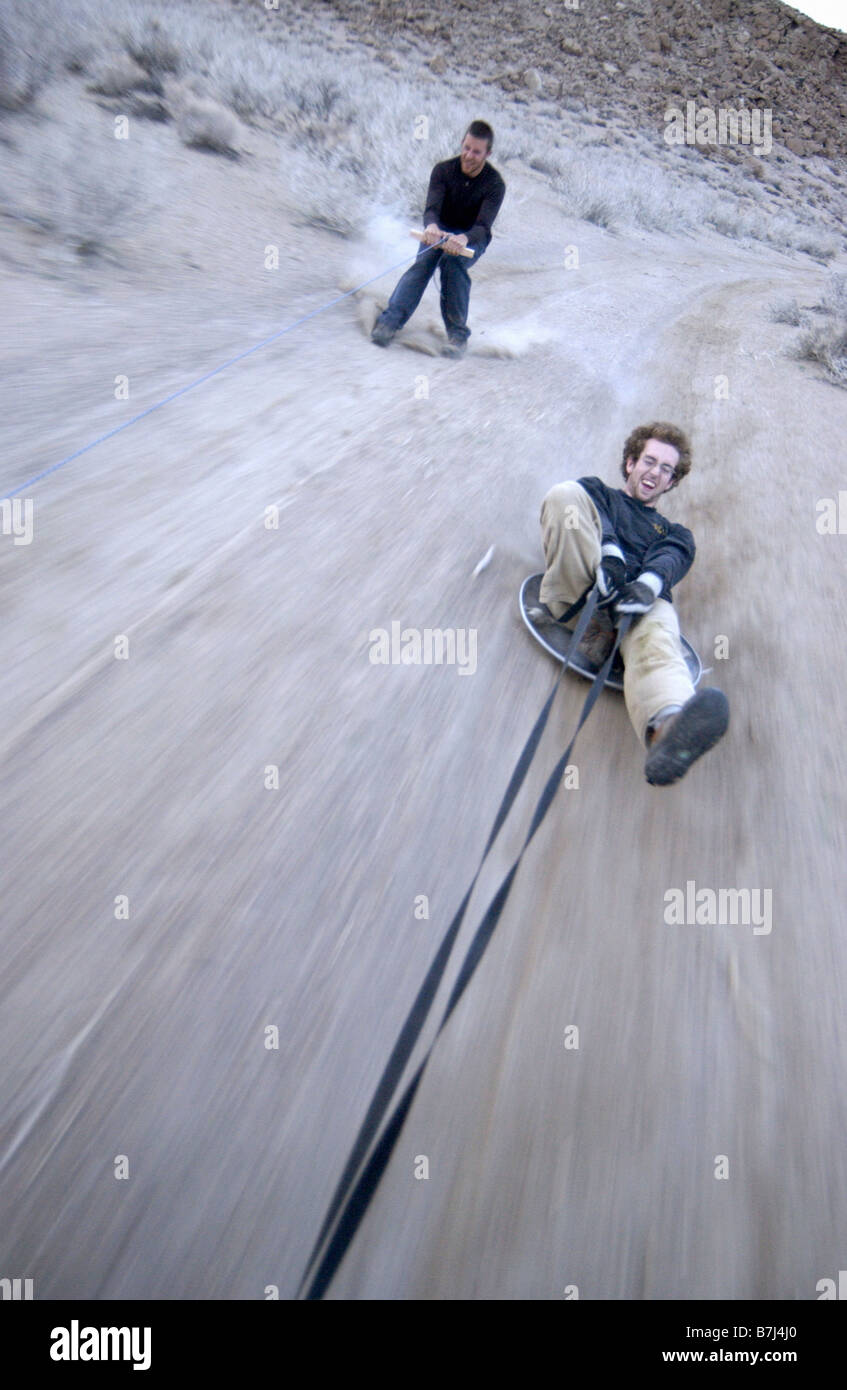 Two men (20-30) surfing behind a car on a dirt road, Bishop, California ...