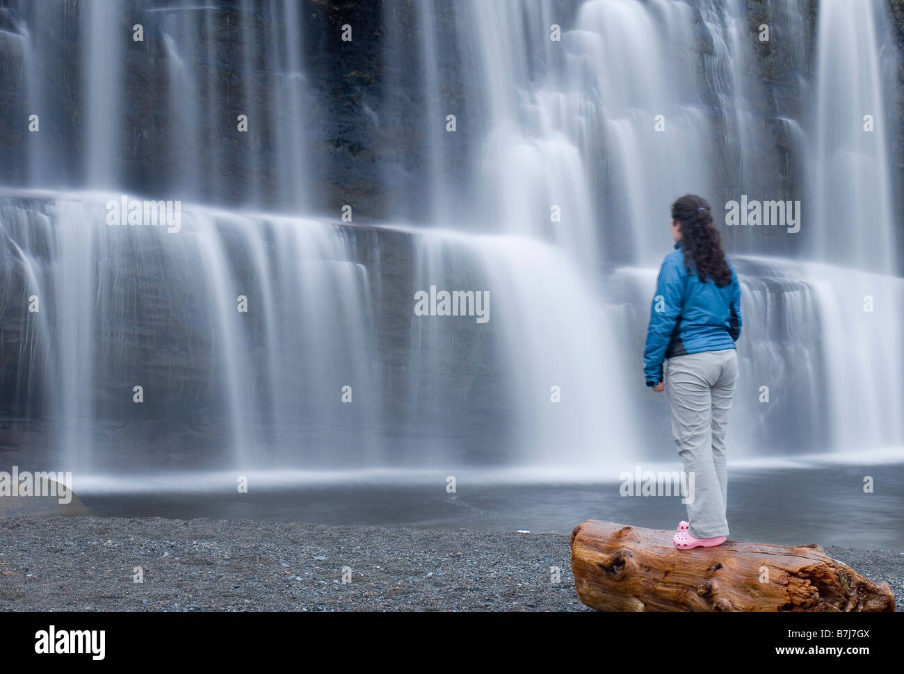 Woman (20-25) standing on a beach log in front of a waterfall Stock ...