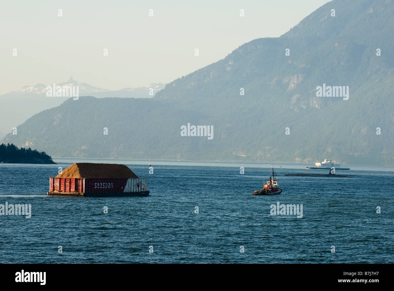 Tug Boat pulling logs through the ocean with mountains in the ...