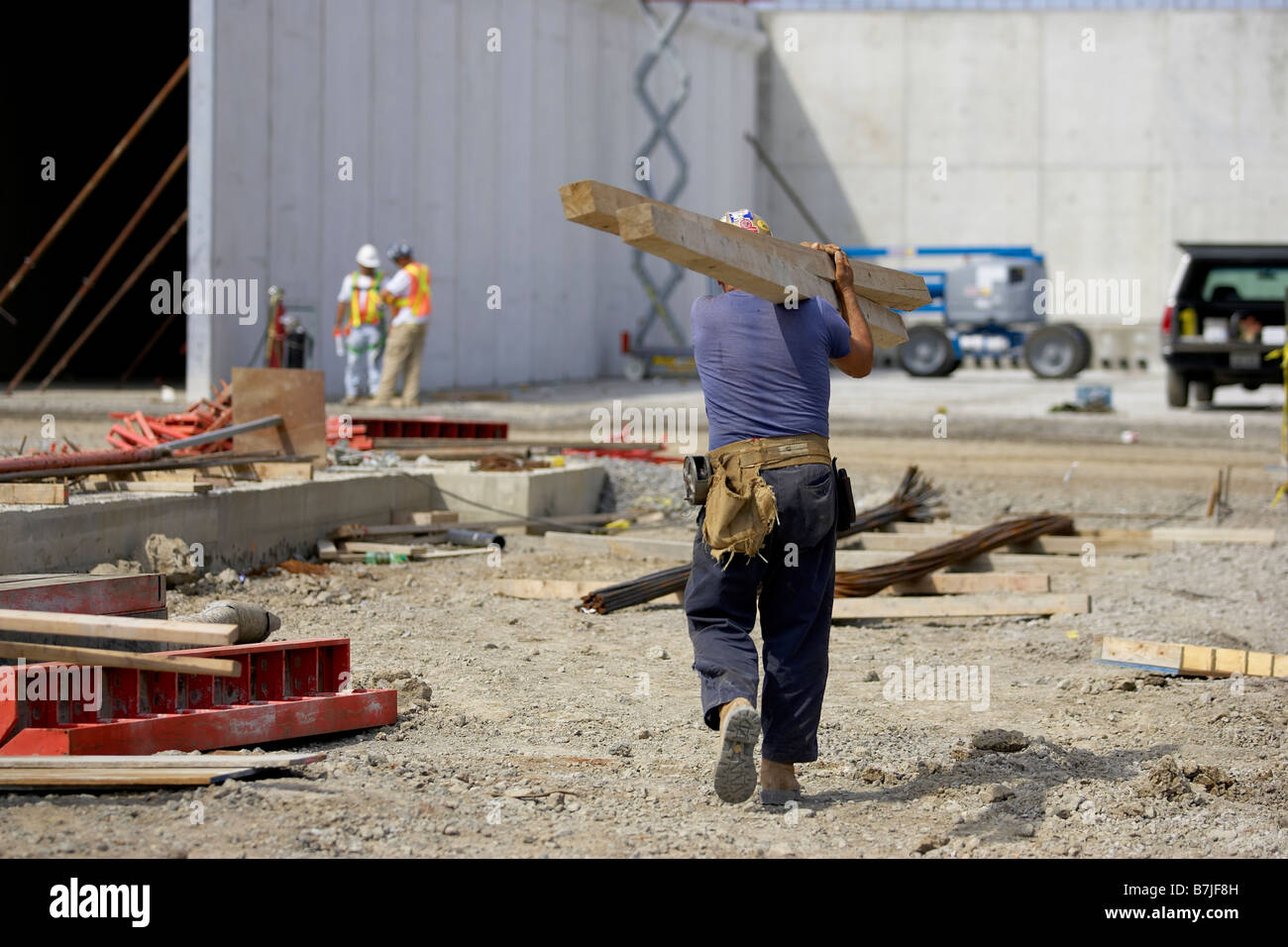 Construction worker carrying wood beams across a construction site ...