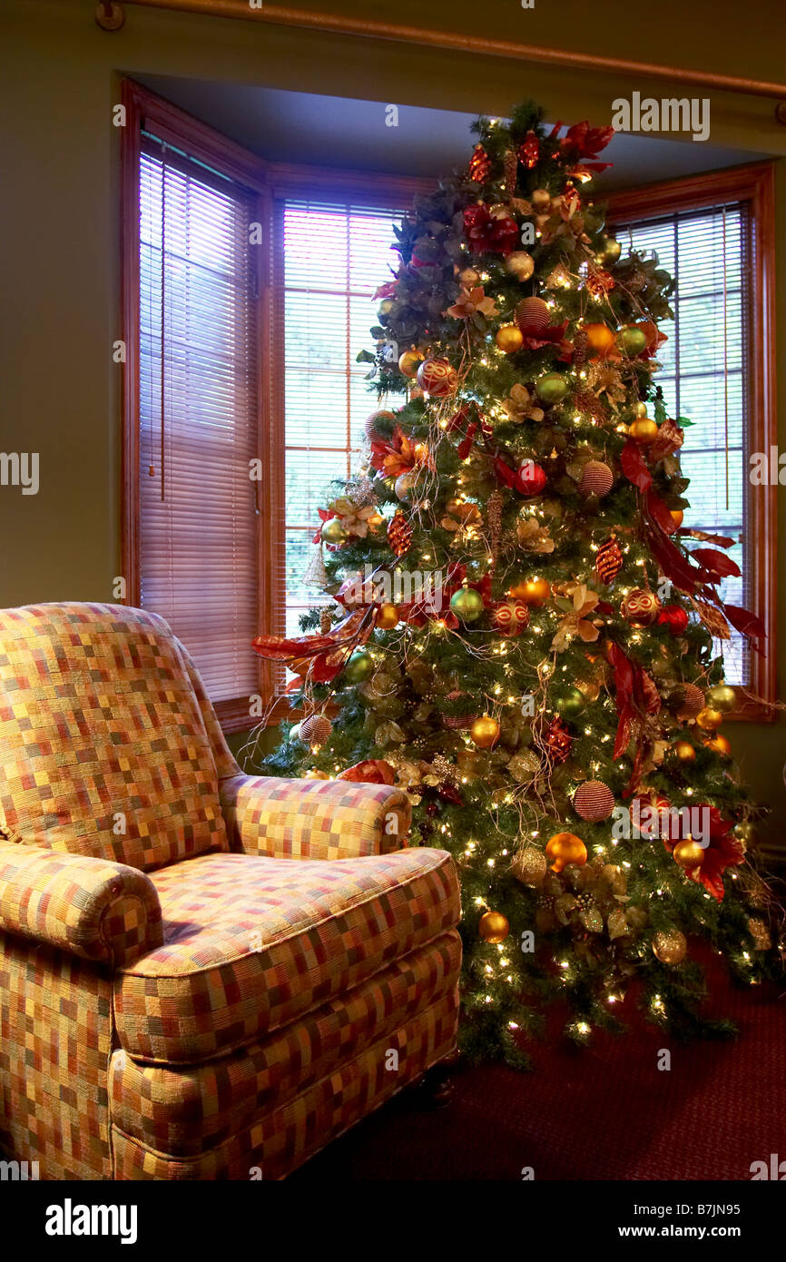 Decorated Christmas tree nestled by the window next to an armchair ...