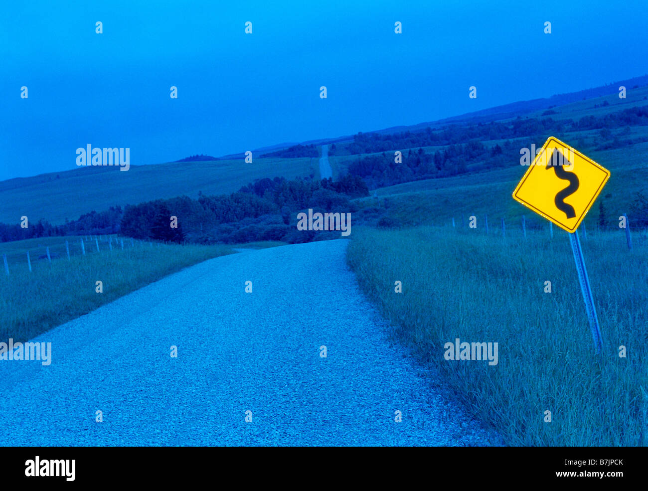 Blue toned winding rural road with bright yellow road sign, Canada ...