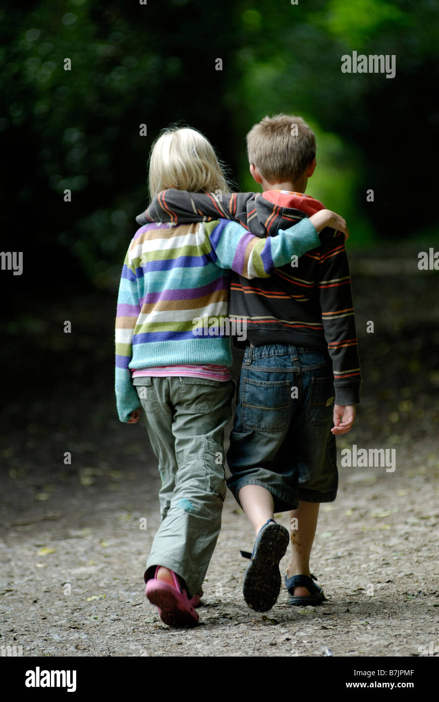 The rear view of a young boy and a girl walking arm in arm through a ...