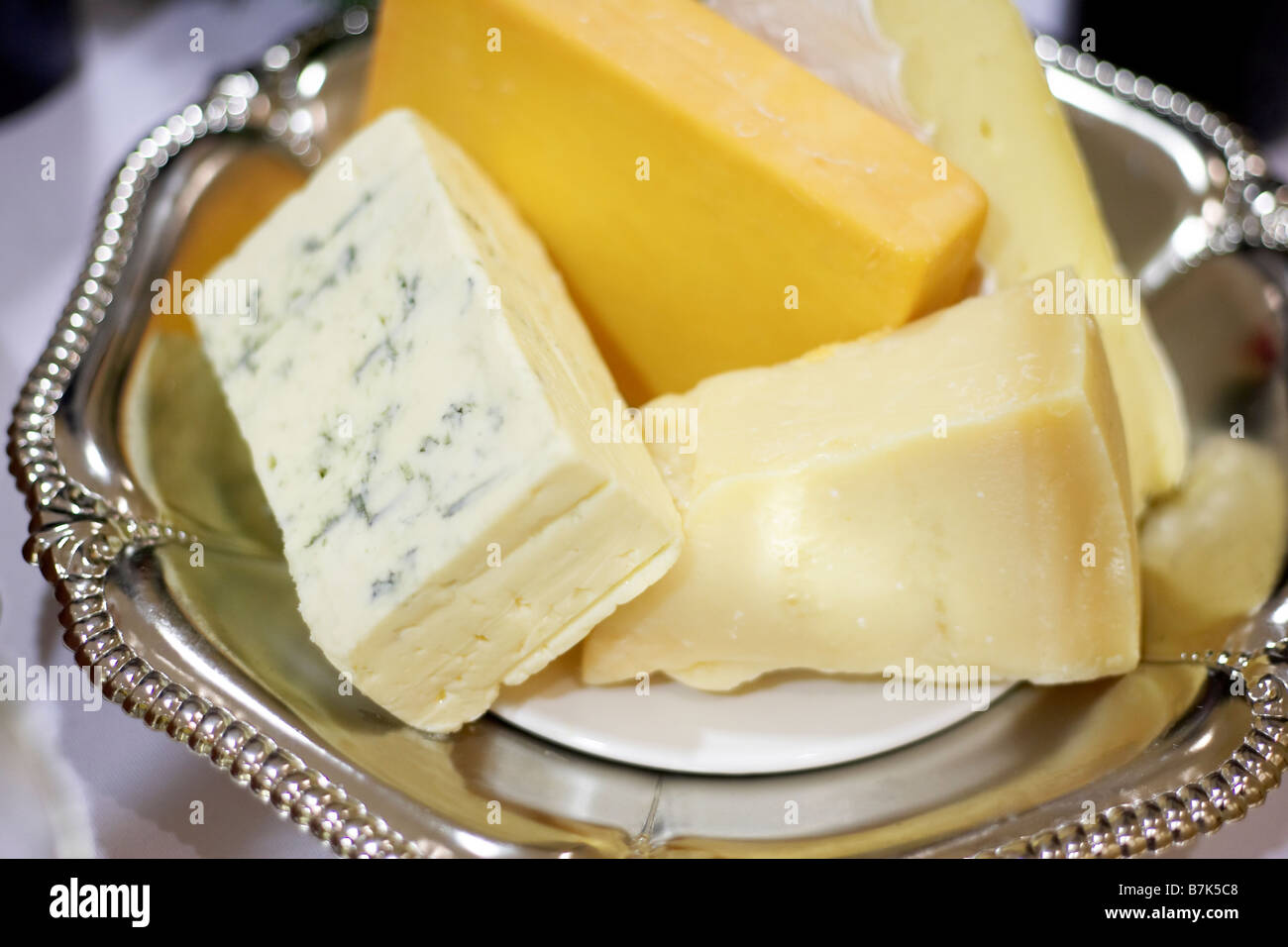 Bricks of blue, cheddar, parmesan, and brie cheese in a silver dish ...