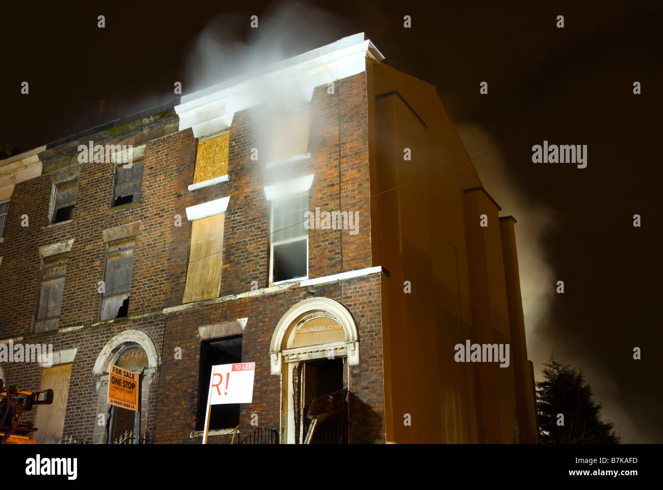 Derelict end terraced Victorian town house on fire at night with smoke ...