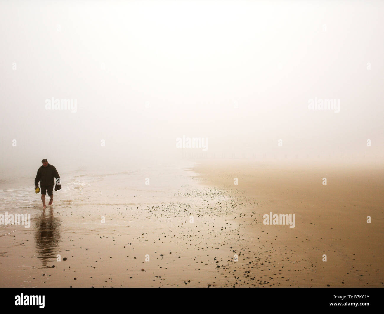 Man walking along beach in fog Stock Photo - Alamy