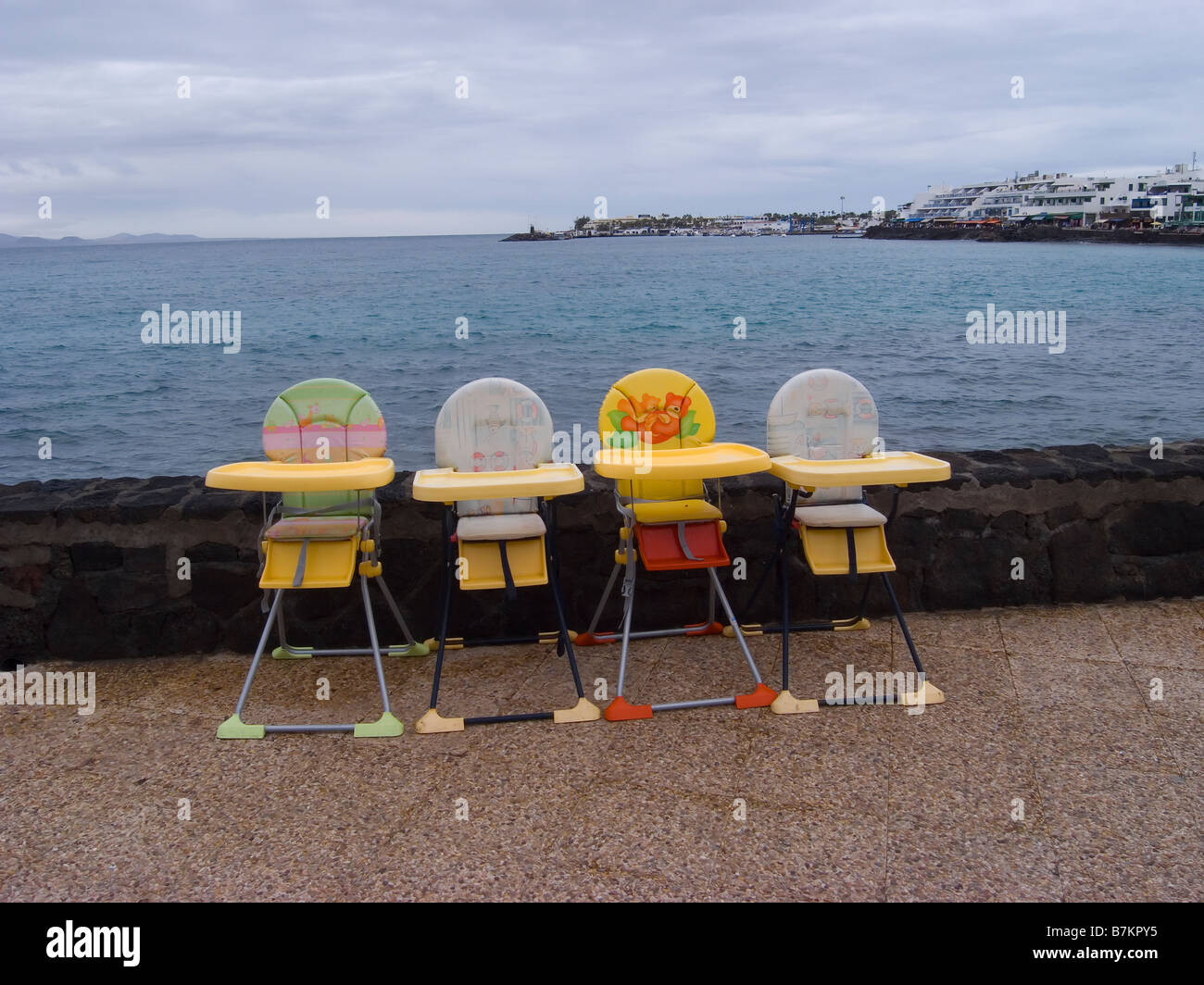 A group of colourful baby chairs lined up ready for use at a seaside ...