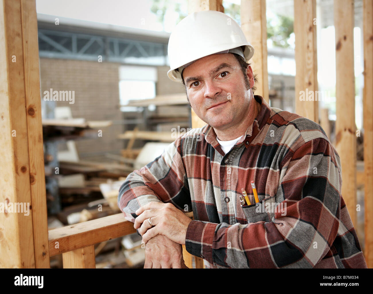A handsome construction worker leaning on the frame of a building he s ...