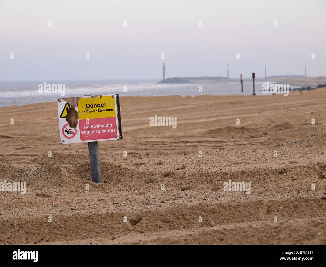 DANGER SIGN PARTLY BURIED UNDER SAND ON BEACH AT ECCLES ON SEA NORFOLK ...