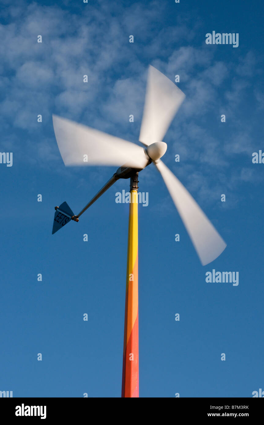 A spinning wind turbine on a blue sky background with white clouds ...