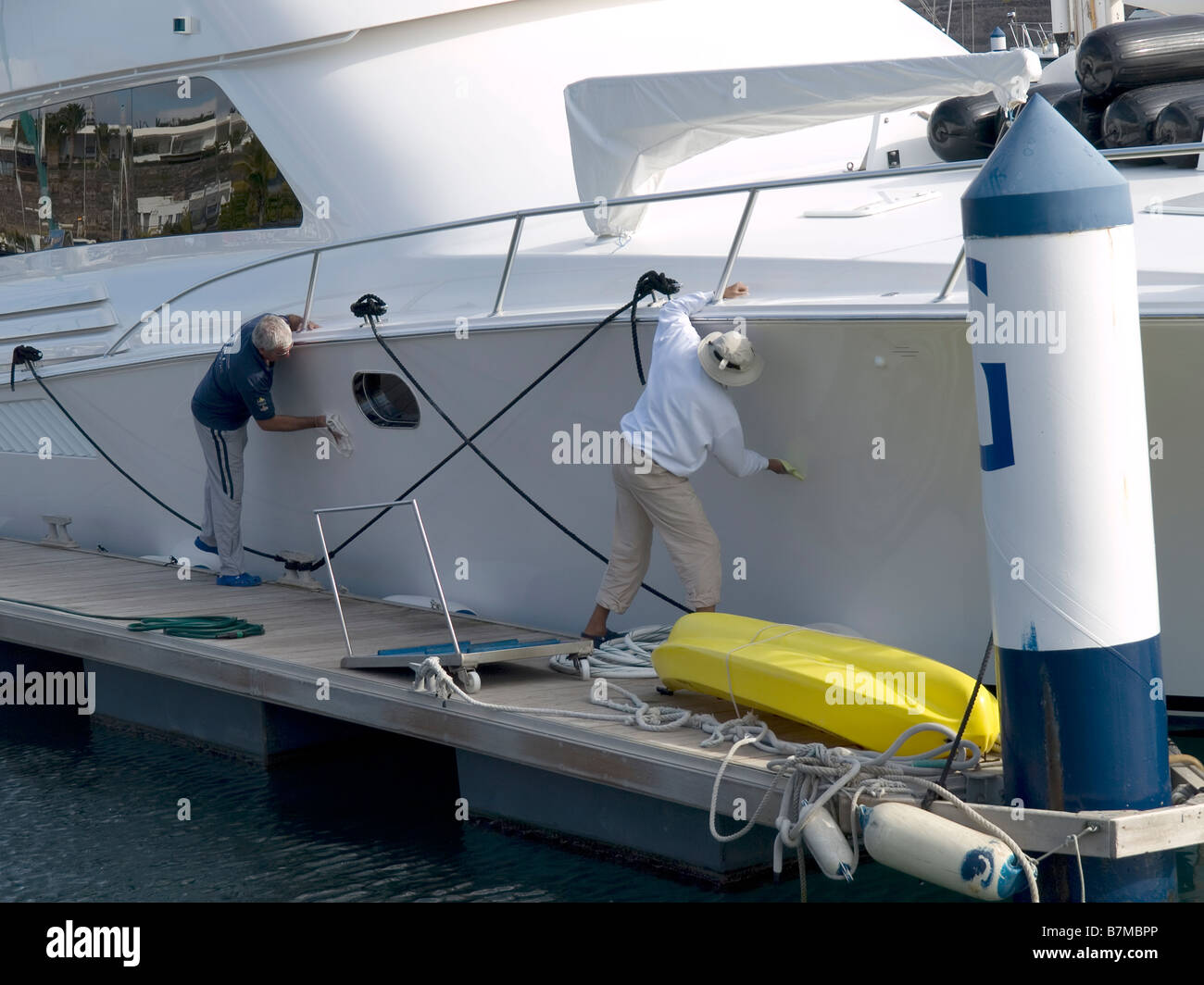 Two men washing the side of a boat at the Puerto Calera yacht marina ...
