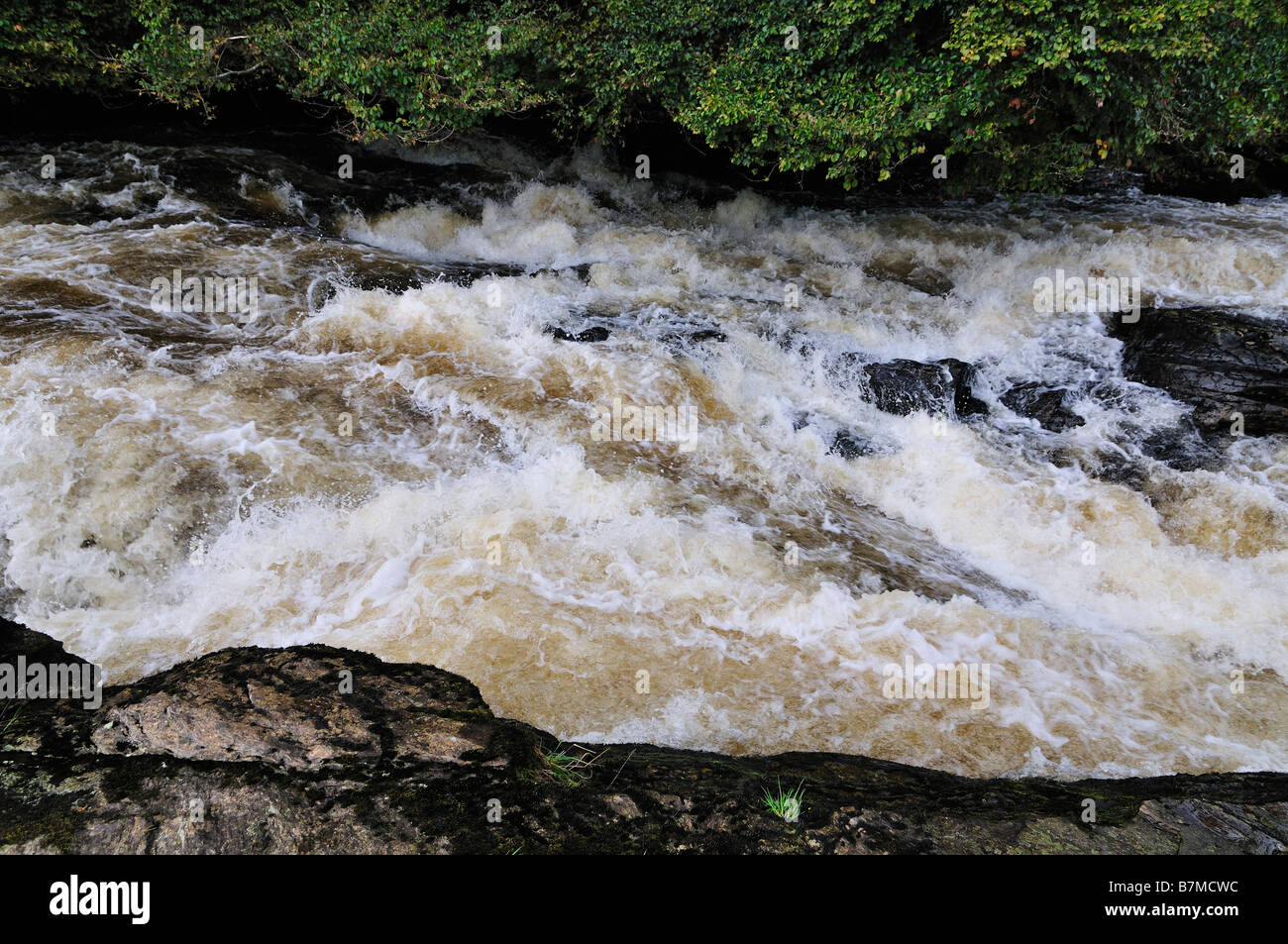 Fast running river in rocky gully with brown floodwater and white ...