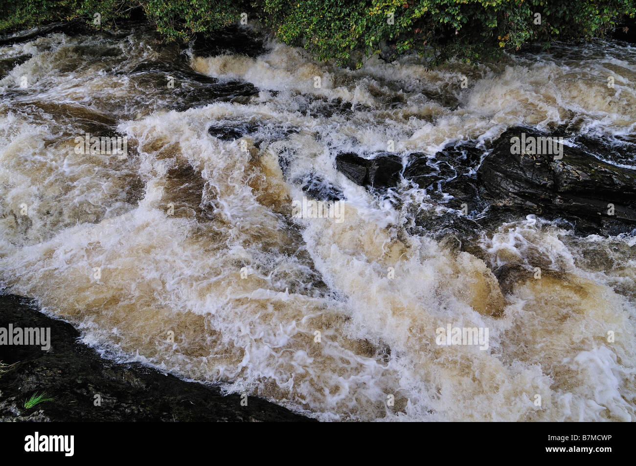 Fast running river in rocky gully with brown floodwater and white ...
