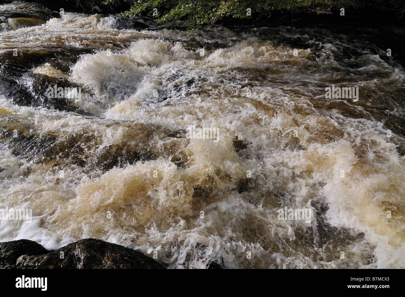 Fast running river in rocky gully with brown floodwater and white ...