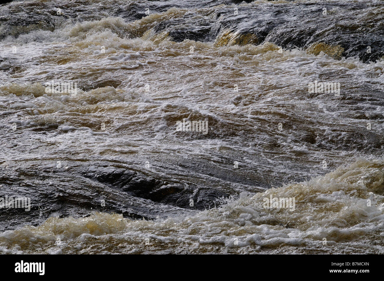 Close up on fast running water with brown floodwater and white rapids ...