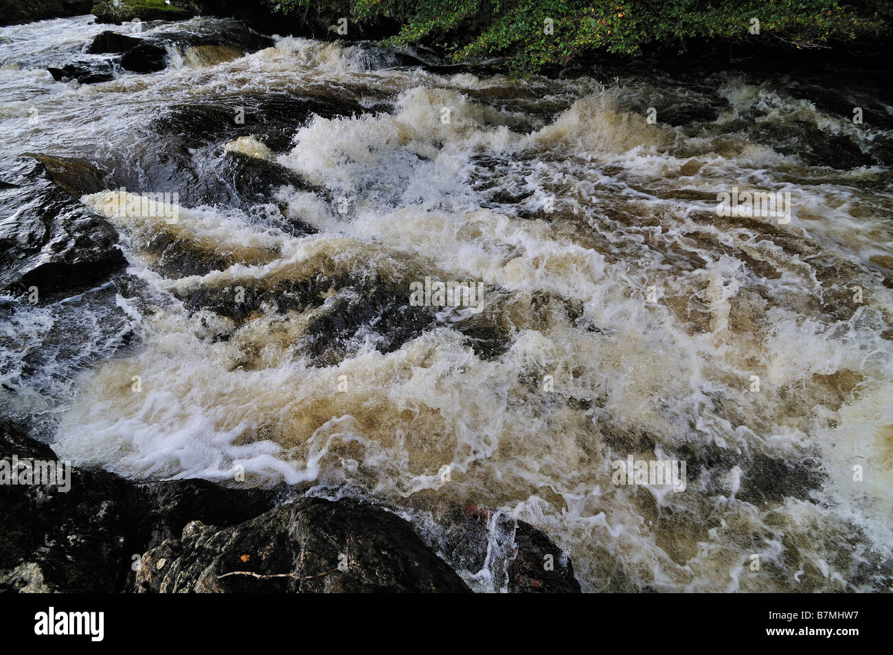Fast running river in rocky gully with brown floodwater and white ...