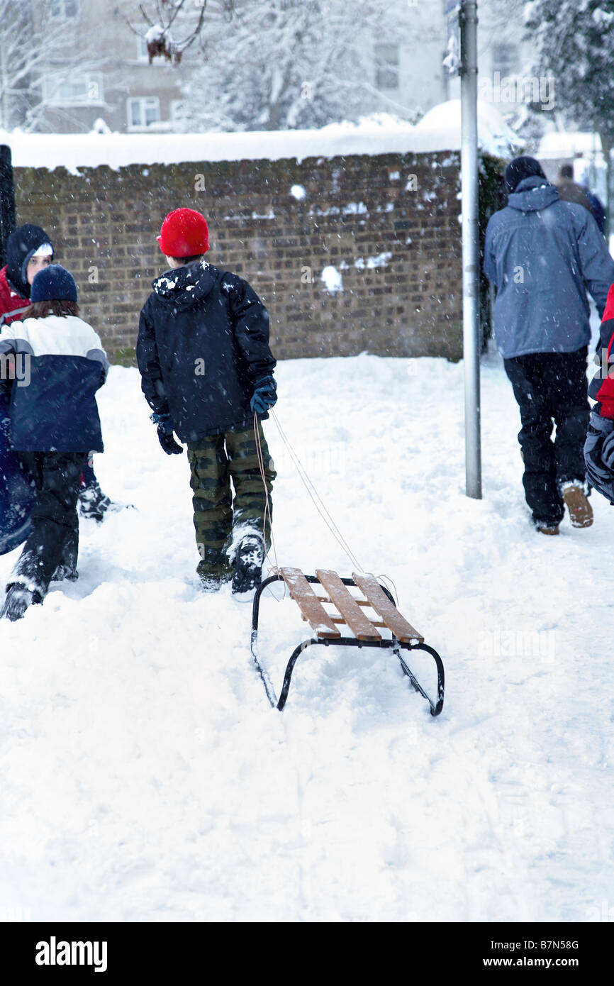 Back view of a young boy wearing a red hat pulling a sledge behind him ...